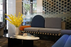 Uma área de recepção moderna com um sofá, um vaso de flores amarelas e uma mesa com um relógio.