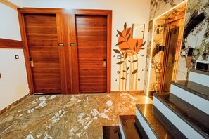 Quarto de hotel com portas duplas de madeira, piso de mármore e escadaria com design moderno.