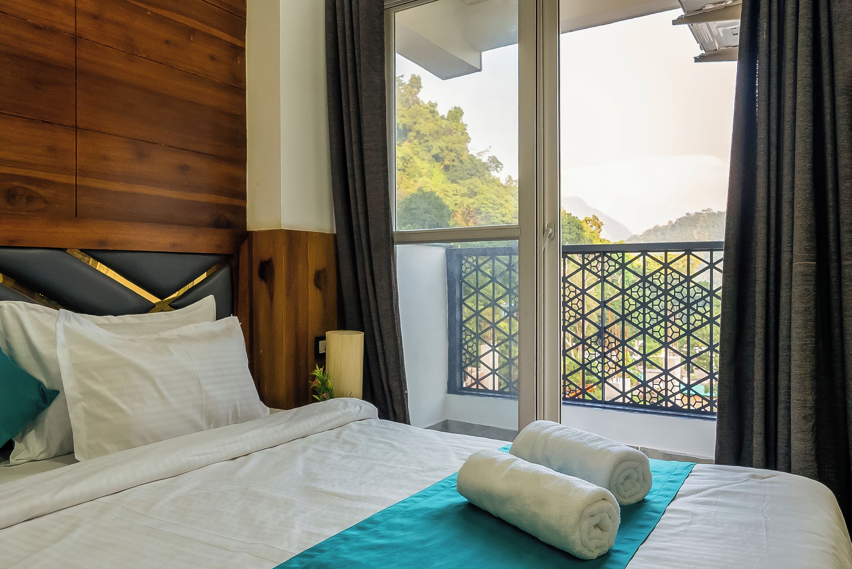 Quarto de hotel com uma cama, vista para o verde pela janela e uma varanda com guarda-corrimão.
