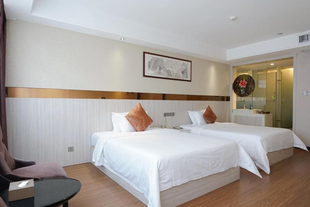 Quarto de hotel com duas camas, área de estar, uma pequena mesa e banheiro visível através de uma porta de vidro.
