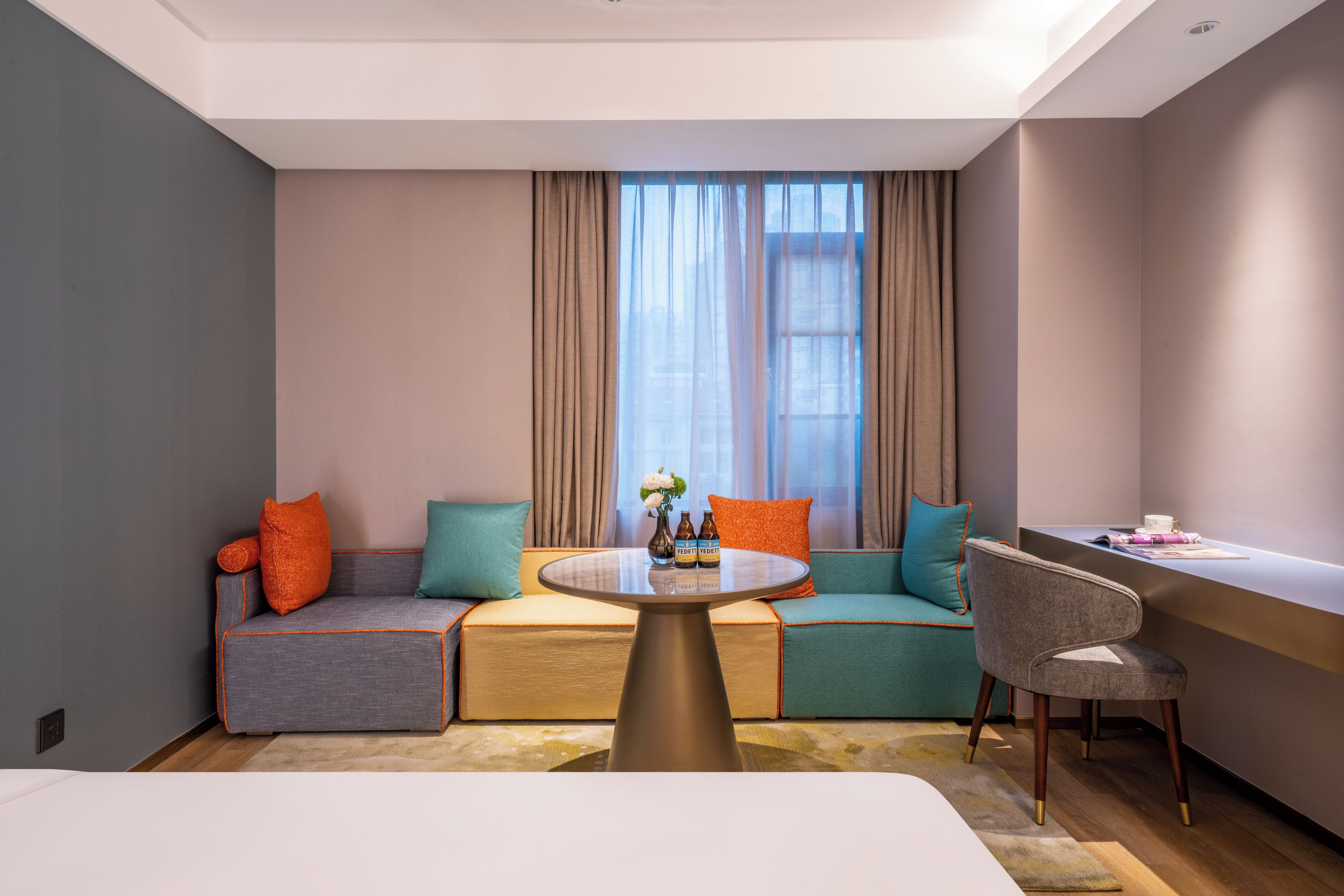 Quarto de hotel moderno com sofá, uma mesa pequena e uma cadeira.
