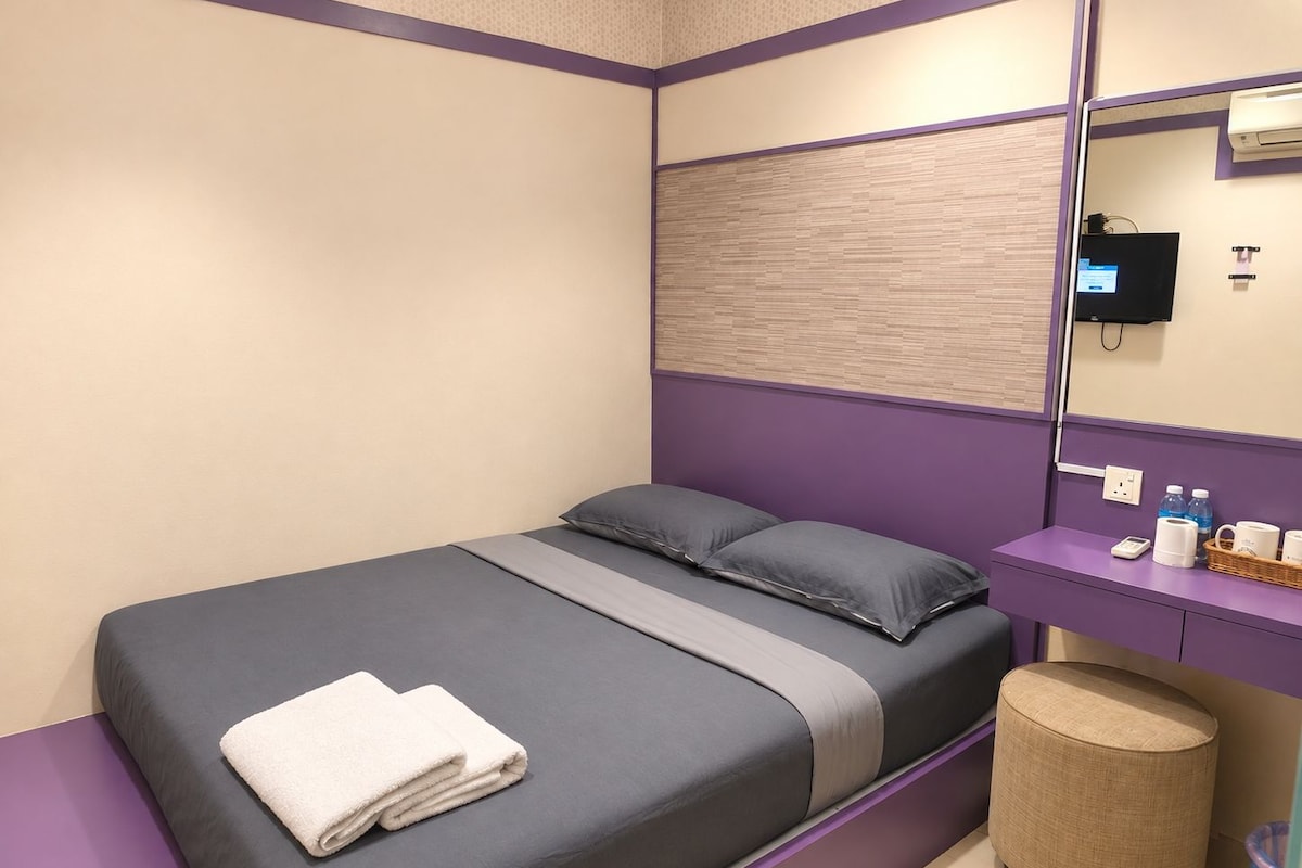 Quarto de hotel com cama, toucador com artigos de higiene e lixeira.