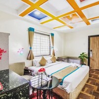 Quarto de hotel com cama, escrivaninha, cadeira, janela com cortinas e claraboia no teto.
