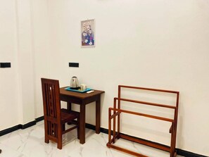 Quarto com uma cadeira de madeira, uma mesa pequena com uma chaleira e uma estrutura de metal na parede.