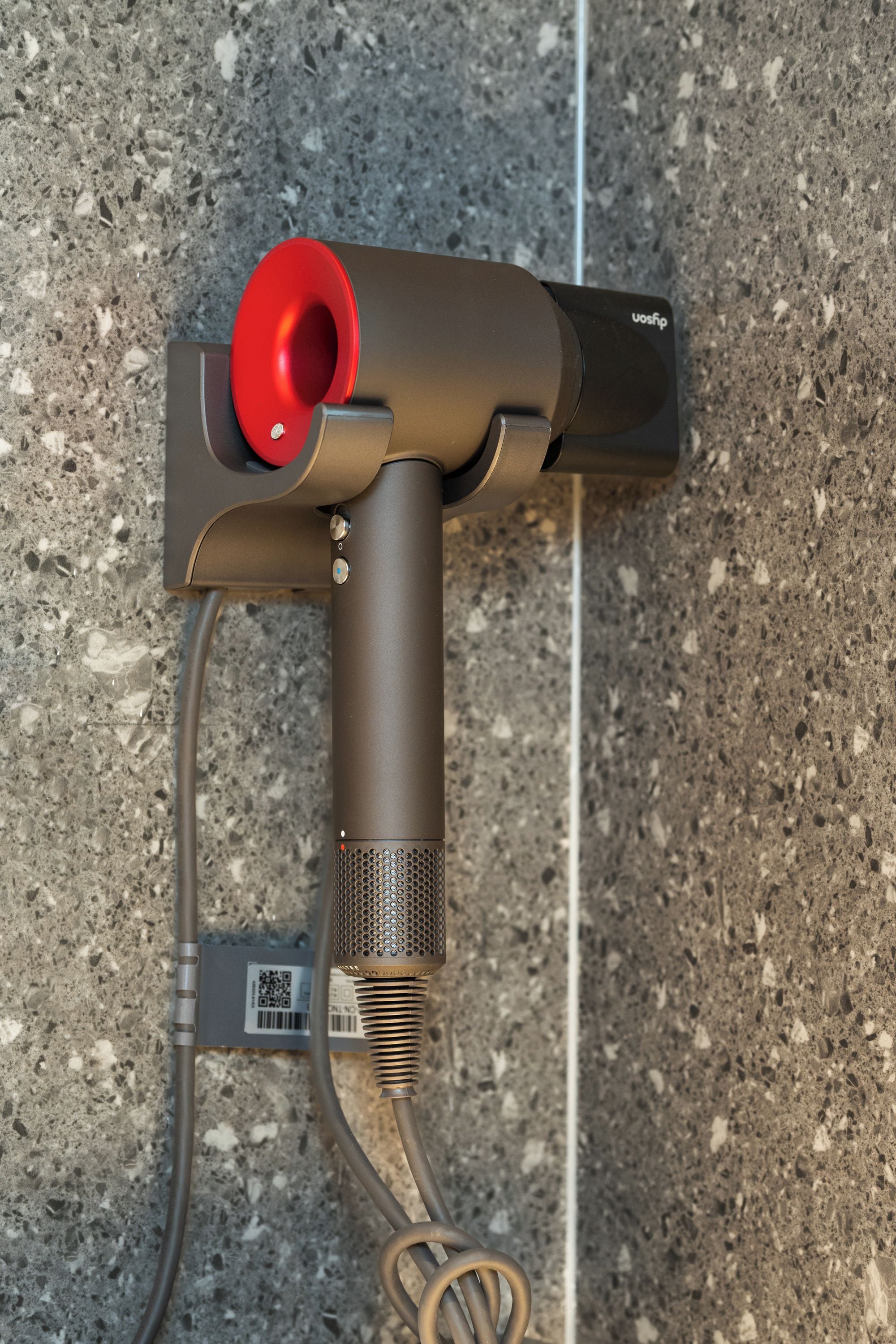 Close-up de um aspirador de pó com um bocal vermelho, um fio e um código QR em uma superfície texturizada.