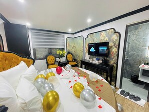 Quarto de hotel com uma cama, televisão, escrivaninha com computador e área de estar com cadeiras.