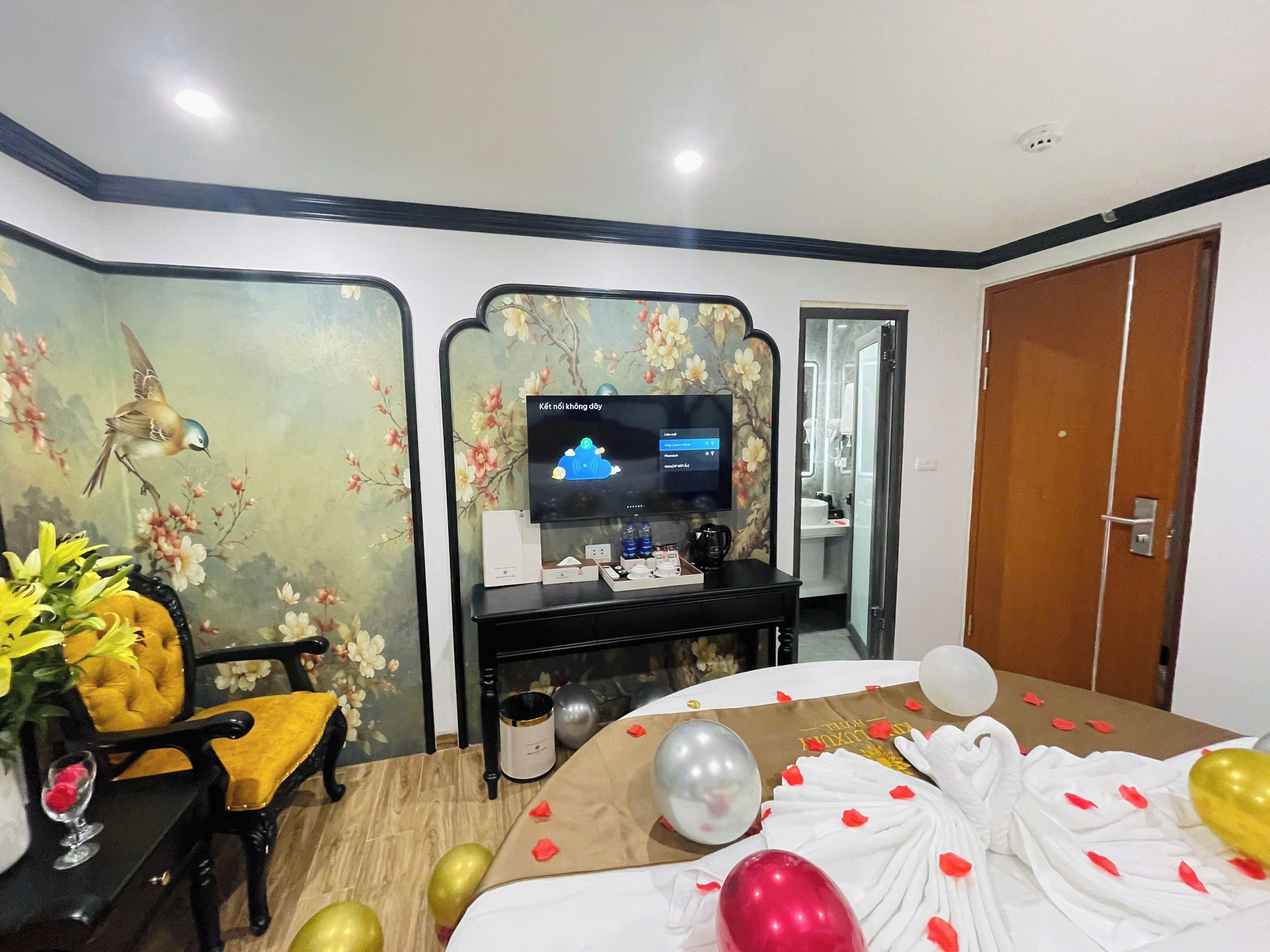 Quarto de hotel com cama, televisão, espelho e papel de parede floral.
