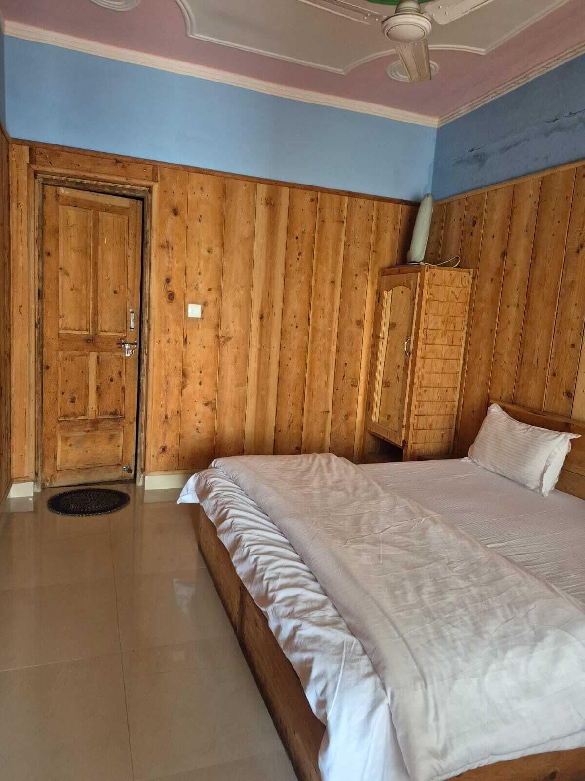 Quarto com painéis de madeira, cama com roupa de cama branca, porta e ventilador de teto.