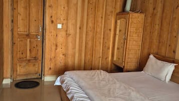 Quarto com painéis de madeira, cama com roupa de cama branca, porta e ventilador de teto.