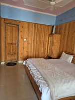Quarto com painéis de madeira, cama com roupa de cama branca, porta e ventilador de teto.