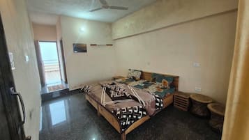 Quarto com cama, ventoinha no teto, porta e pequena janela.