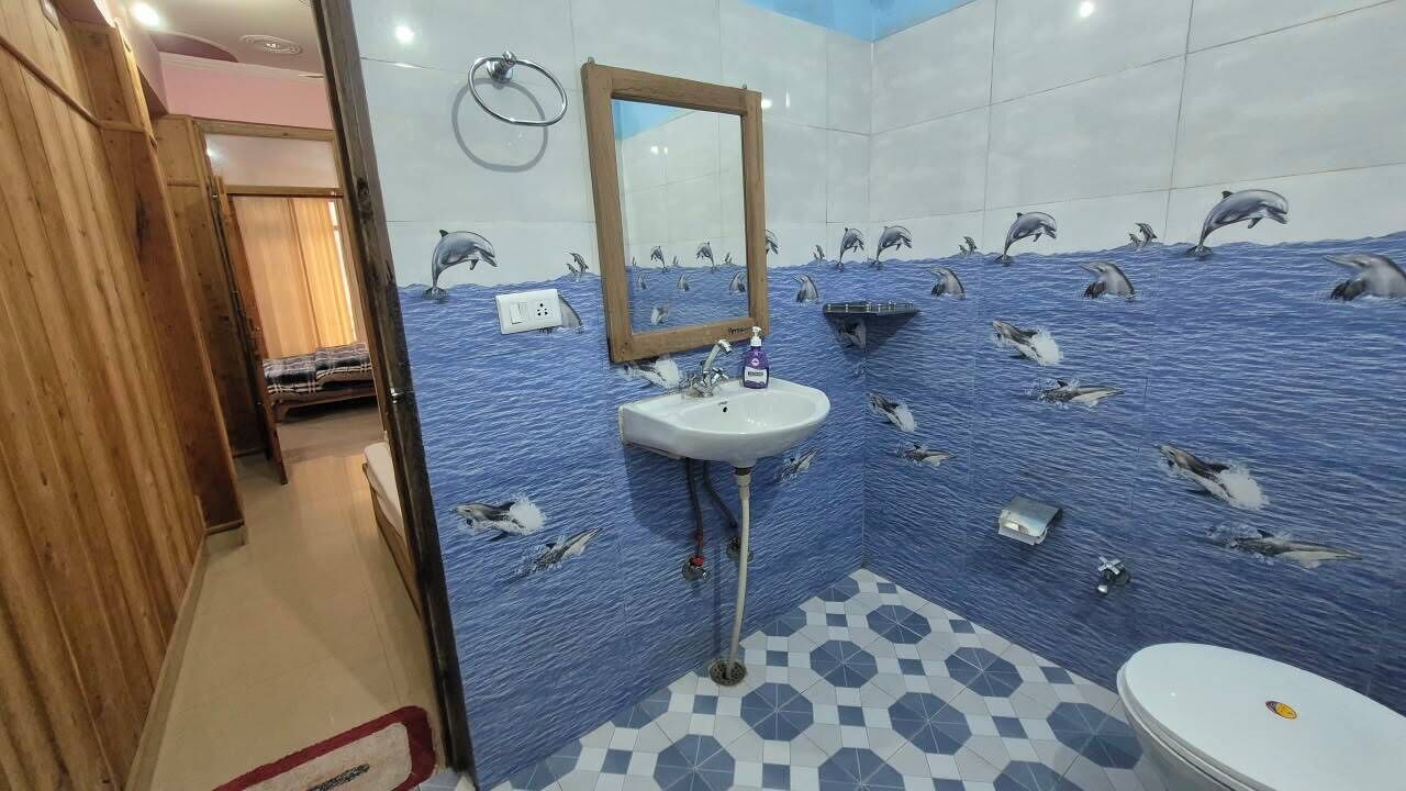 Casa de banho com parede revestida em azulejos azuis, lavatório, espelho e sanita.