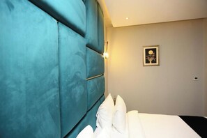 Quarto de hotel com uma cama grande, cabeceira verde-água, luminária fixada na parede e um quadro emoldurado.