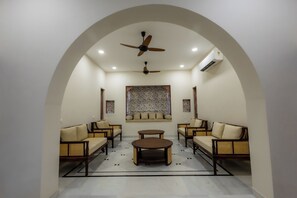 Quarto com teto abobadado, duas ventoinhas de teto, uma mesa redonda central e quatro sofás dispostos ao redor.