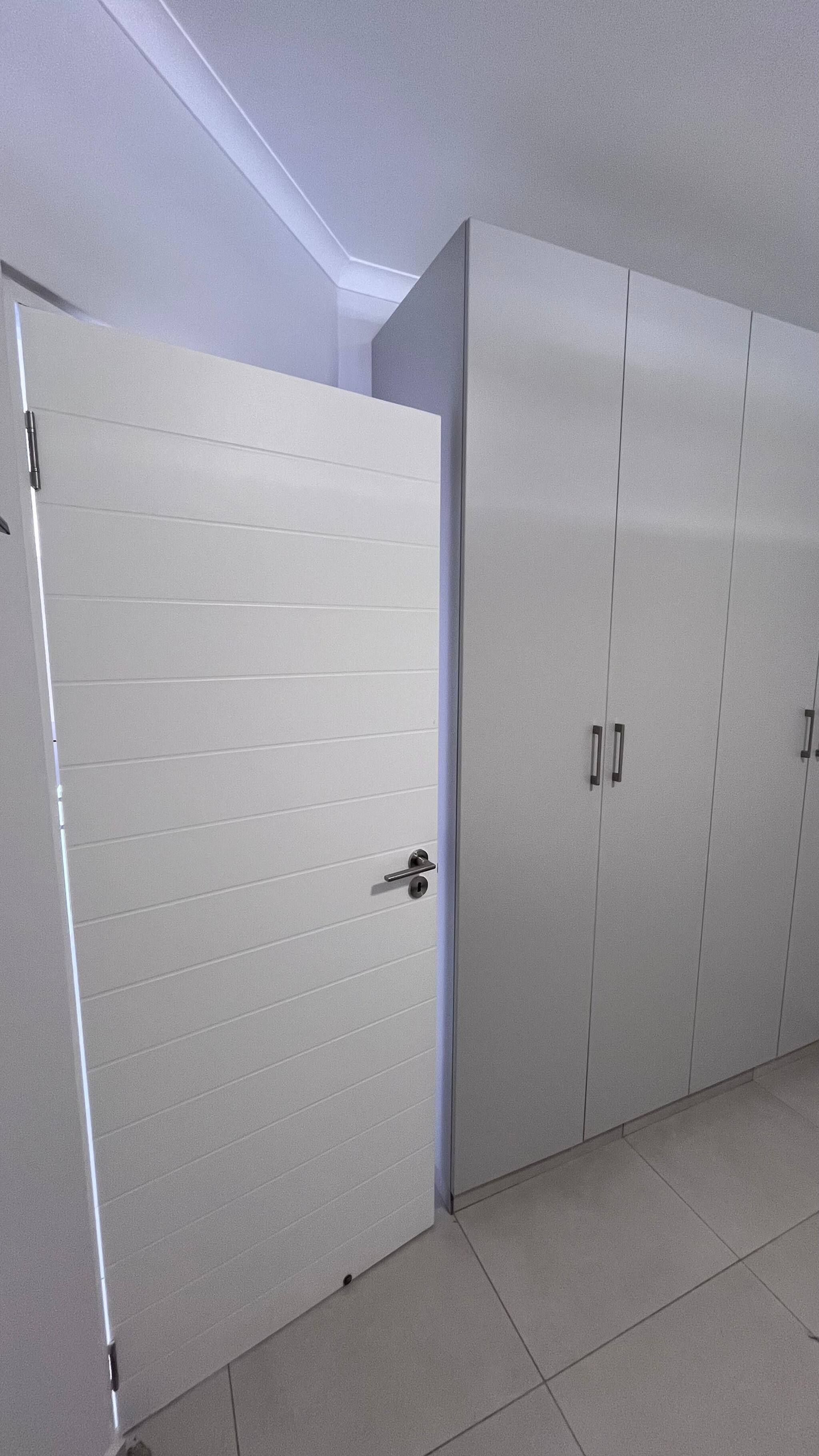 Quarto com porta branca, guarda-roupa e chão em azulejos.
