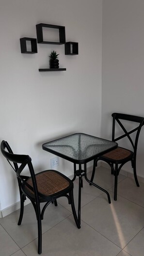 Quarto de canto com mesa de vidro e duas cadeiras com assentos trançados.