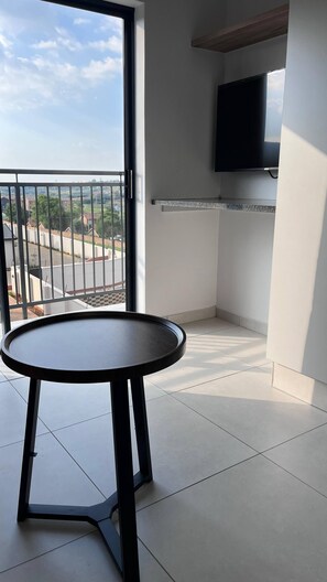 Uma varanda com uma mesa redonda, uma TV fixada na parede e vista para o exterior.