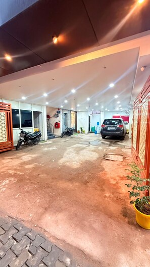 Área de estacionamento coberta com carro e motocicletas, escada e porta dando acesso a um edifício.
