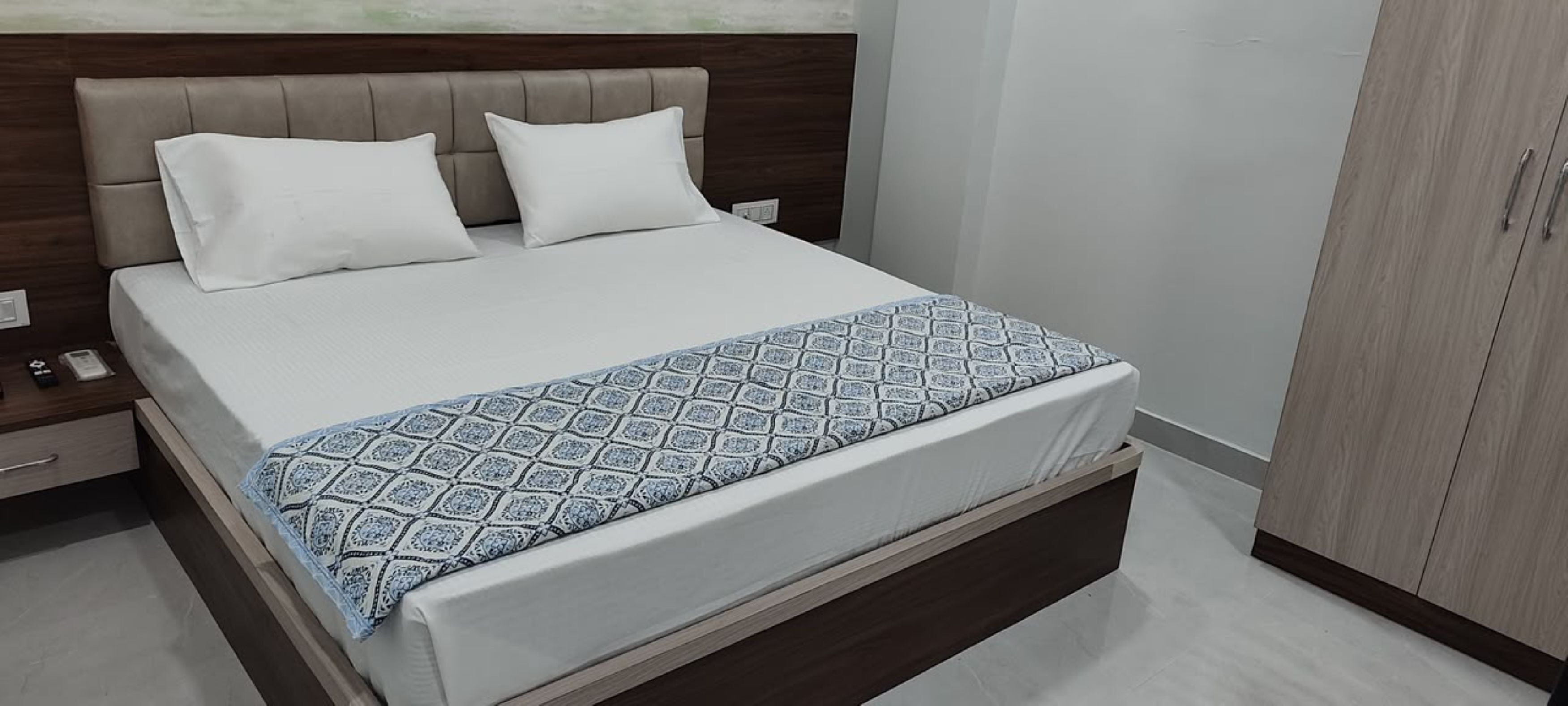 Uma cama com manta estampada, cabeceira de madeira e mesa de cabeceira com gaveta.