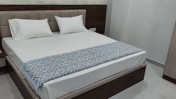 Uma cama com manta estampada, cabeceira de madeira e mesa de cabeceira com gaveta.