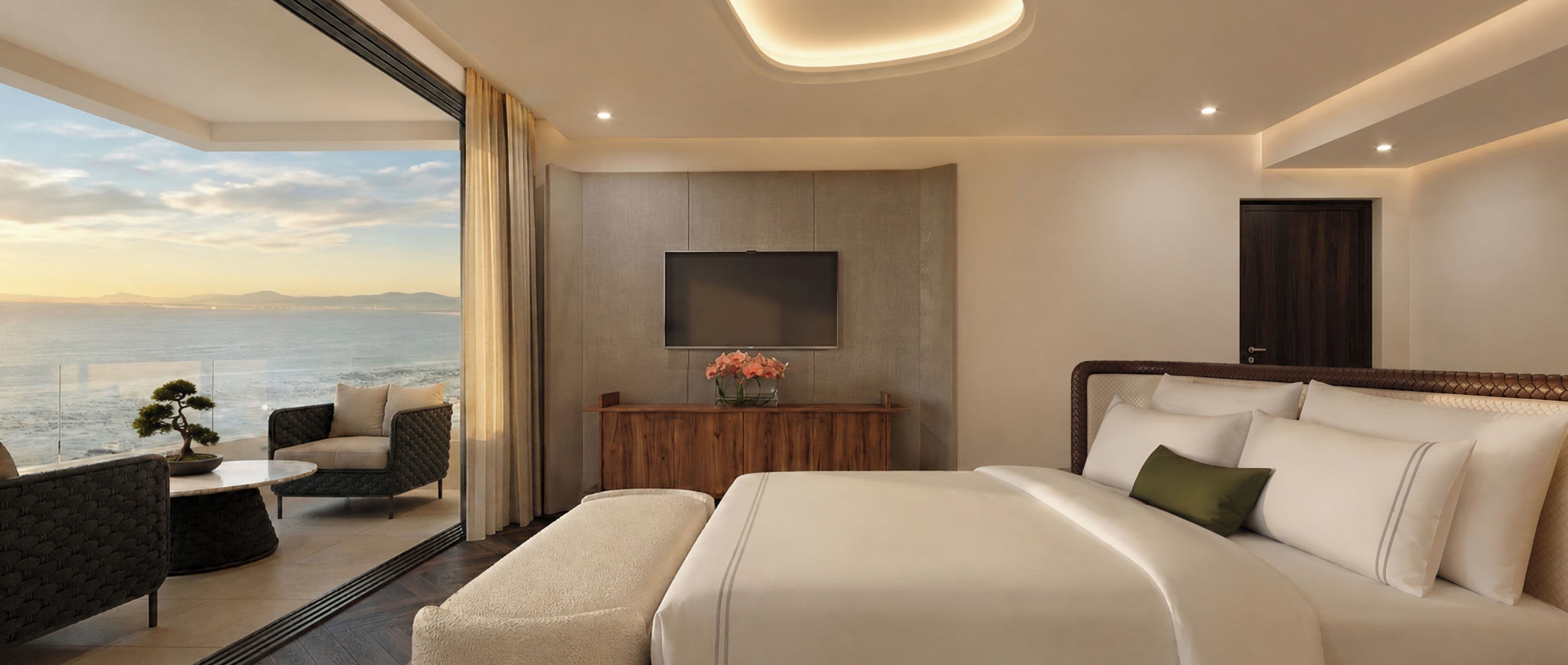 Quarto de hotel com uma cama, área de estar com mesa, TV na parede e vista para o mar.