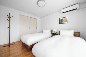 Quarto de hotel com duas camas, um cabideiro, ar-condicionado, mesa de cabeceira com abajur e um quadro na parede.