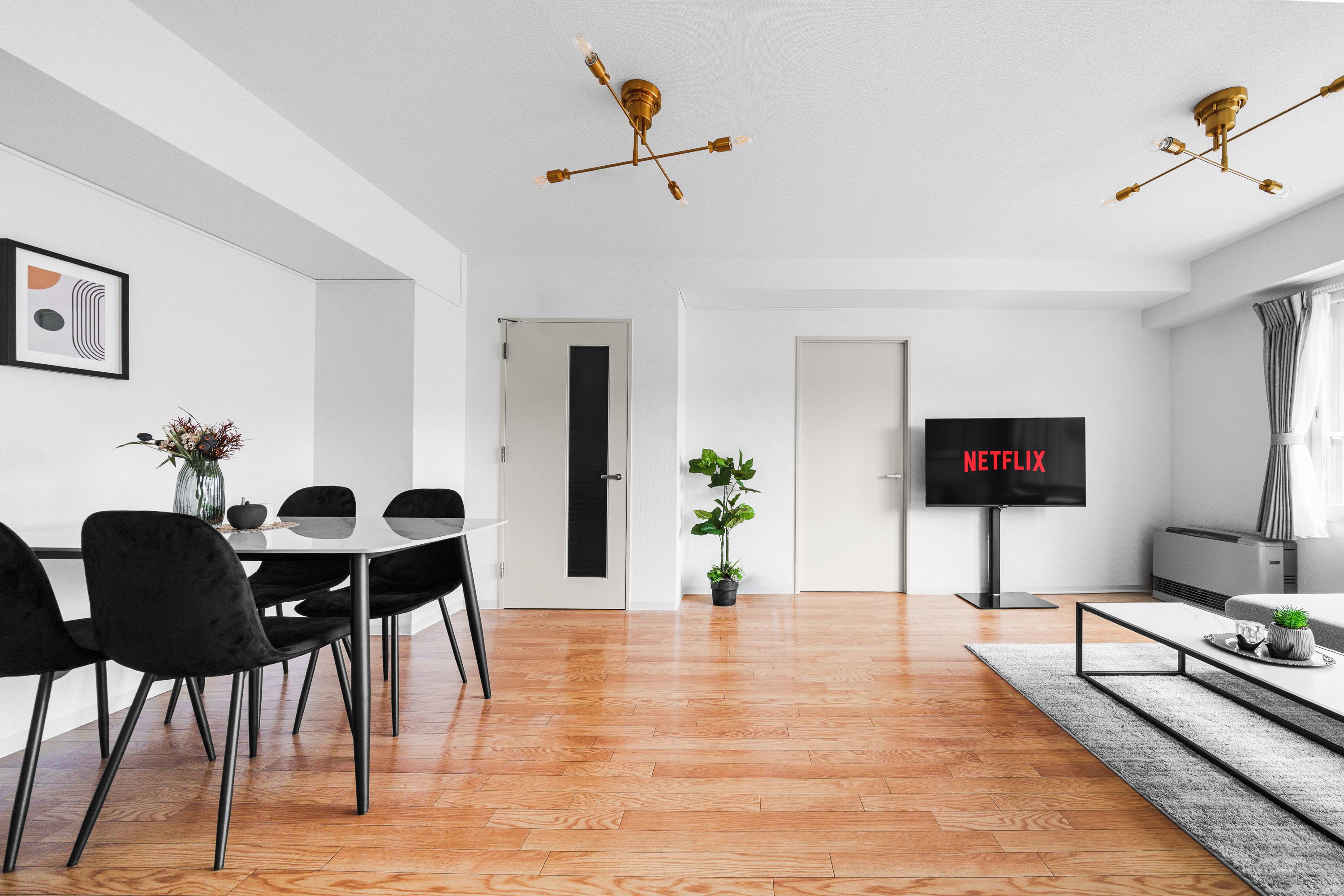 Uma sala de estar moderna com área de jantar, televisão de tela plana e luminária no teto.