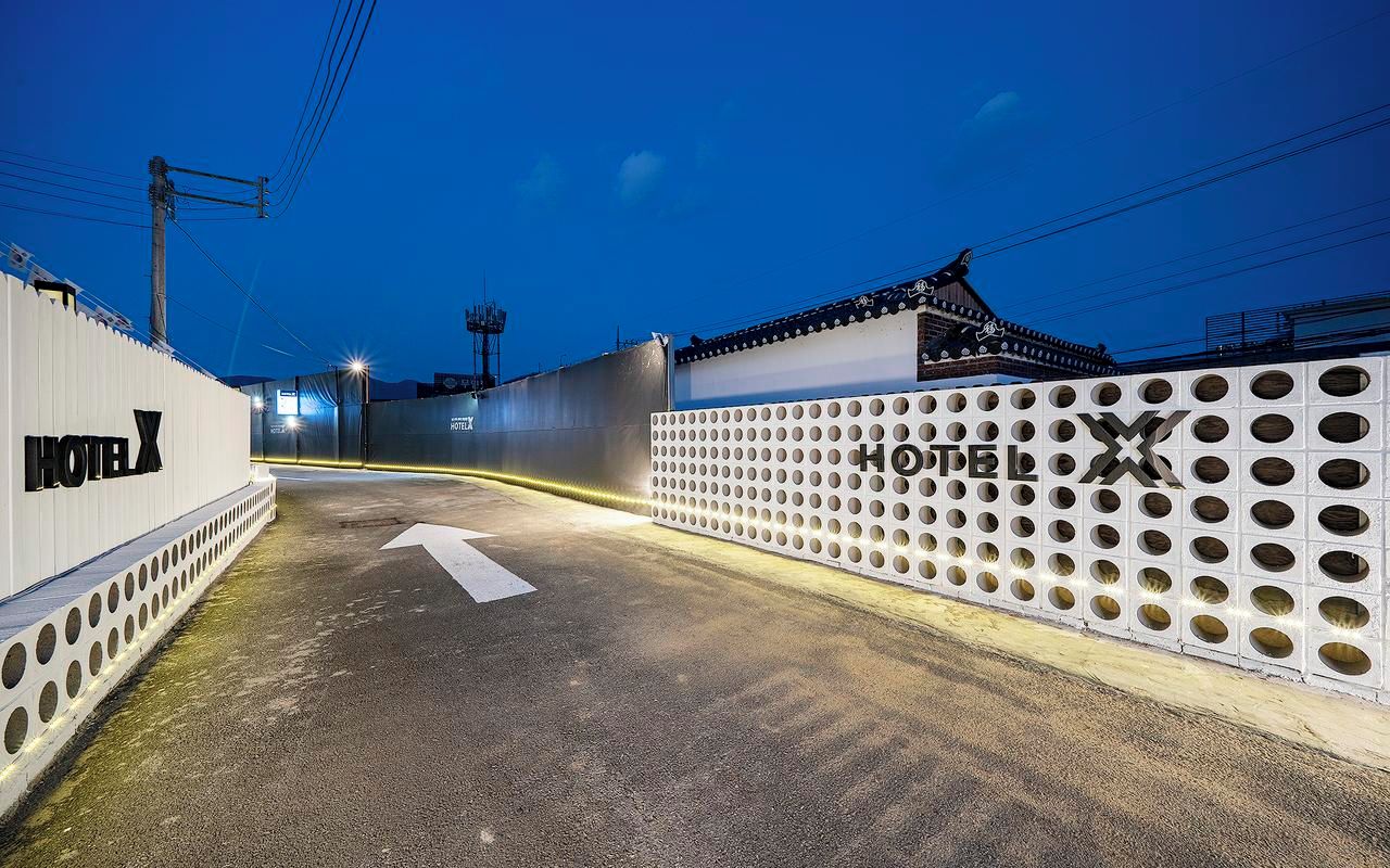 Entrada de hotel com um portão tradicional e uma cerca moderna com aberturas circulares.