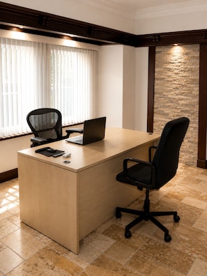 Uma sala de conferências com uma mesa de madeira, duas cadeiras de escritório pretas, um laptop e um telefone.
