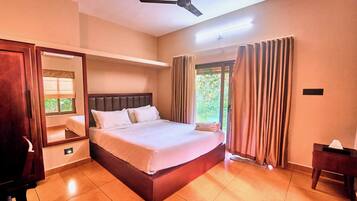 Quarto de hotel com uma cama grande, ventoinha no teto, janela com cortinas e mesa de cabeceira.