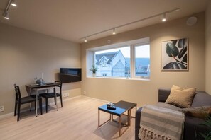 Sala de estar com sofá, mesa de centro, televisão e janela com vista para uma casa.