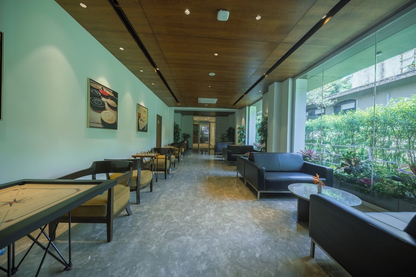 Amplo espaço interno com mesa de bilhar, áreas de estar e vista para um jardim exuberante através de grandes janelas.