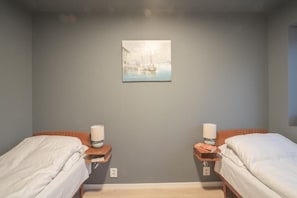 Quarto de hotel com duas camas, um quadro na parede e mesas de cabeceira com luminárias e livros.