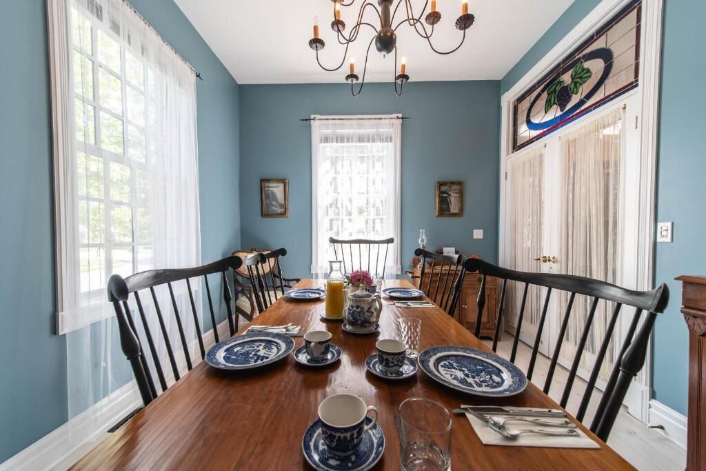 Uma sala de jantar com uma longa mesa de madeira posta para refeição, rodeada por cadeiras.