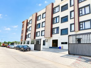 Um edifício residencial com vários andares, portão de entrada e área de estacionamento.