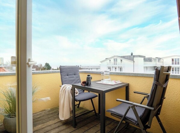 Varanda com mesa, duas cadeiras, planta em vaso e vista para edifícios.