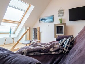 Quarto com teto inclinado, cama com manta estampada em formato de estrela, televisão e pintura do oceano.