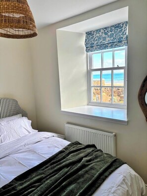 Quarto com cama, janela e vista para a praia, além de radiador.