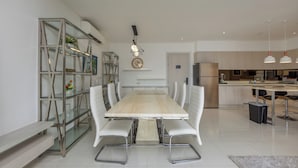 Cozinha moderna com ilha central, eletrodomésticos de aço inoxidável e área de jantar com mesa comprida e cadeiras brancas.