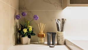 Uma bancada de banheiro com produtos de higiene, um vaso de flores e um espelho.