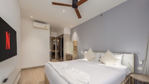 Quarto de hotel com cama, ventoinha no teto, televisão presa na parede e escrivaninha com cadeira.
