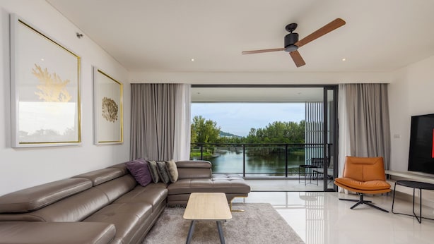 Uma sala de estar moderna com sofá seccional, mesa de centro, TV e varanda com vista para o verde.