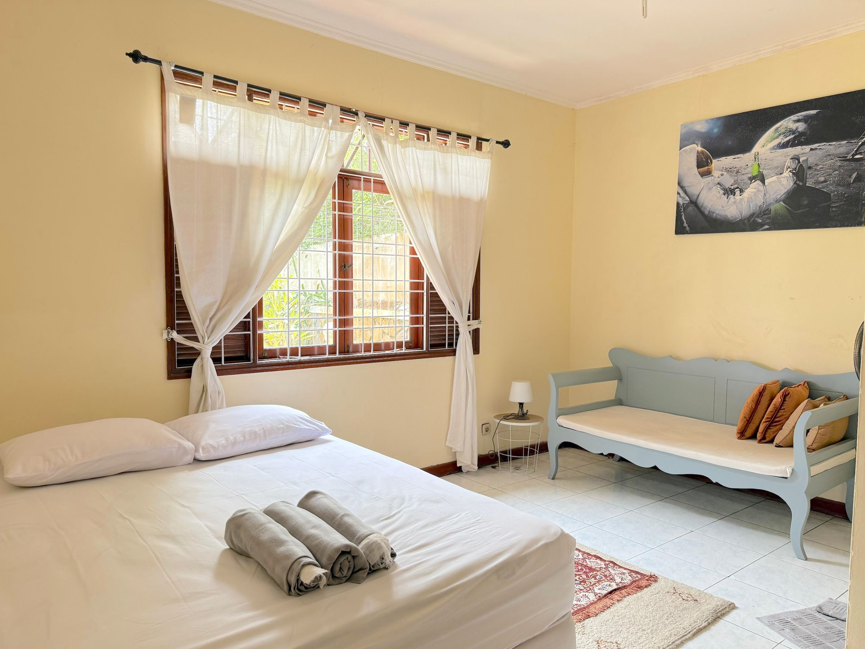 Quarto de hotel com cama, janela com cortinas, sofá e um quadro na parede.