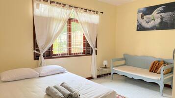 Quarto de hotel com cama, janela com cortinas, sofá e um quadro na parede.