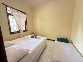 Um pequeno alojamento com uma única sala, duas camas, uma janela com cortina e uma parede simples.