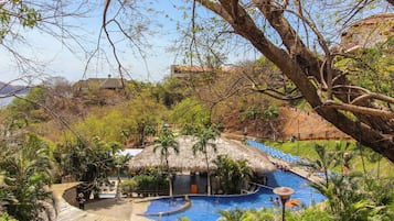 Uma área de piscina com estrutura de telhado de palha, cercada por palmeiras e espreguiçadeiras.