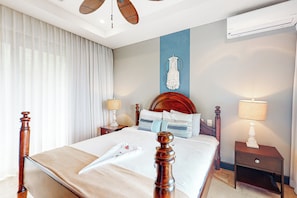 Quarto de hotel com cama, mesa de cabeceira, luminária, ar-condicionado fixado na parede e janela com cortinas.