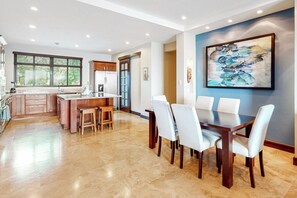 Uma cozinha moderna com uma ilha central, uma área de jantar com mesa grande e cadeiras, e uma sala de estar com uma grande pintura abstrata na parede.