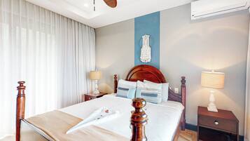 Quarto de hotel com cama, mesa de cabeceira, luminária, ar-condicionado fixado na parede e janela com cortinas.