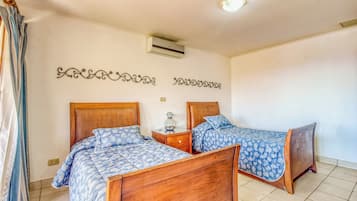 Quarto com duas camas de madeira, uma pequena mesa de cabeceira com um recipiente de vidro e um objeto decorativo na parede.